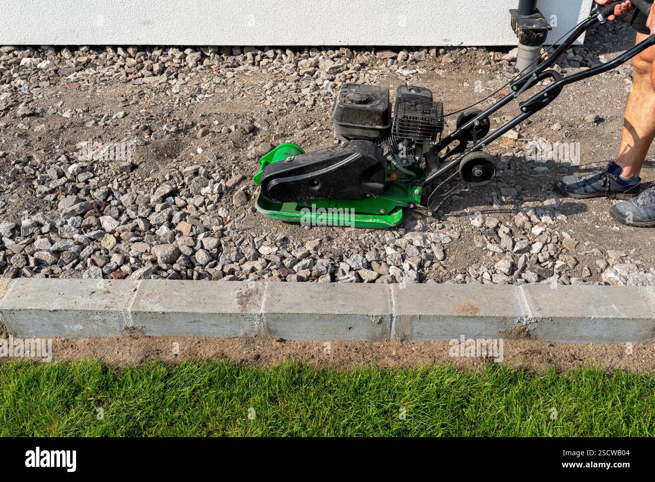A man compacts rubble on a terrace under construction using a hand-held ...