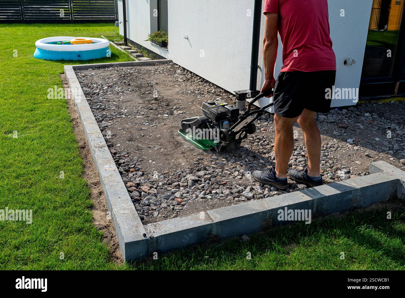 A man compacts rubble on a terrace under construction using a hand-held ...