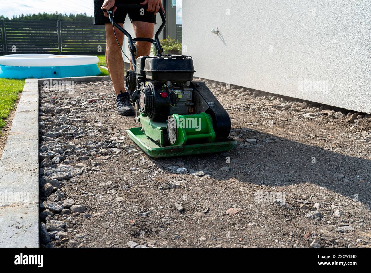 A man compacts rubble on a terrace under construction using a hand-held ...