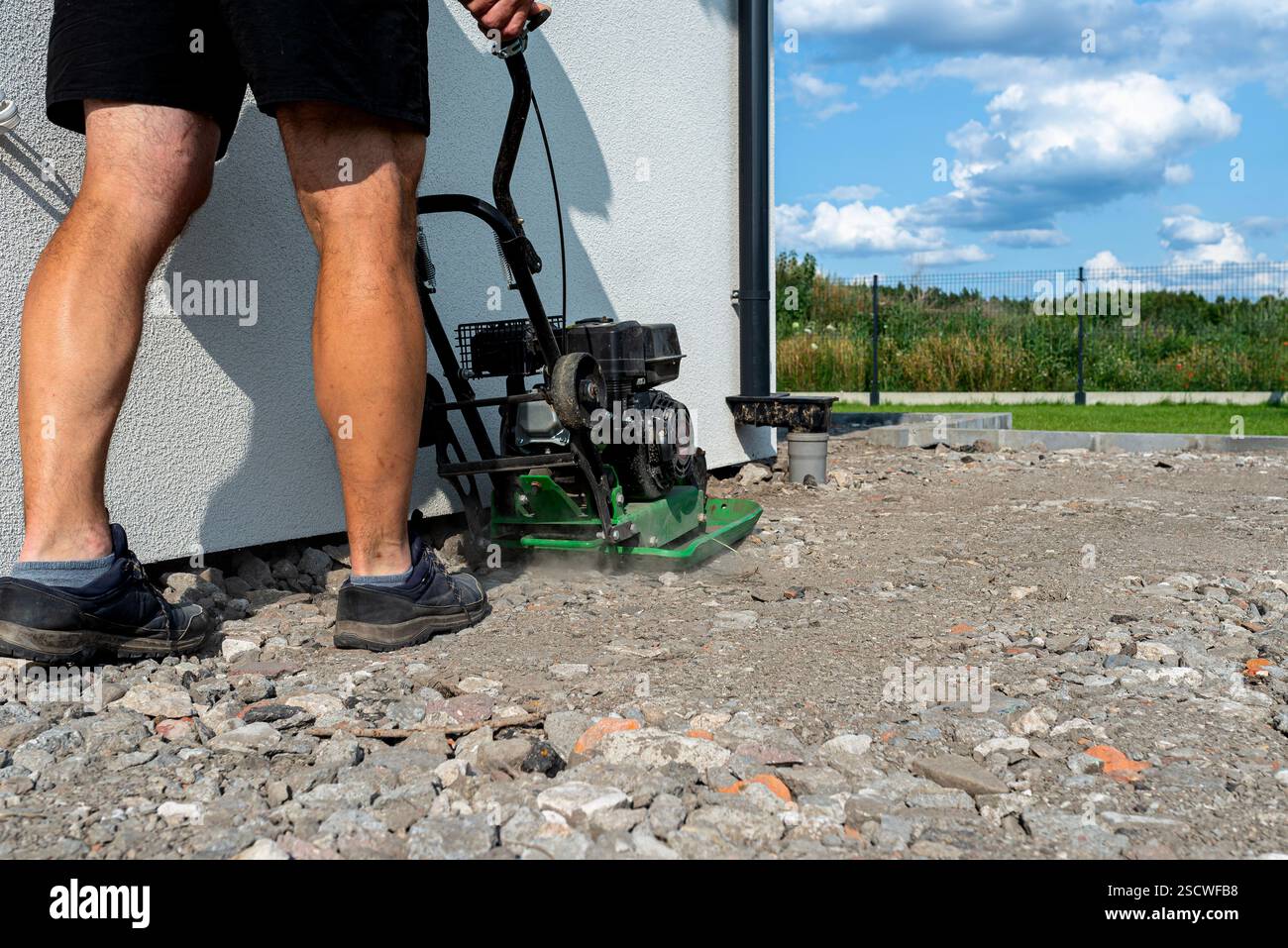 A man compacts rubble on a terrace under construction using a hand-held ...