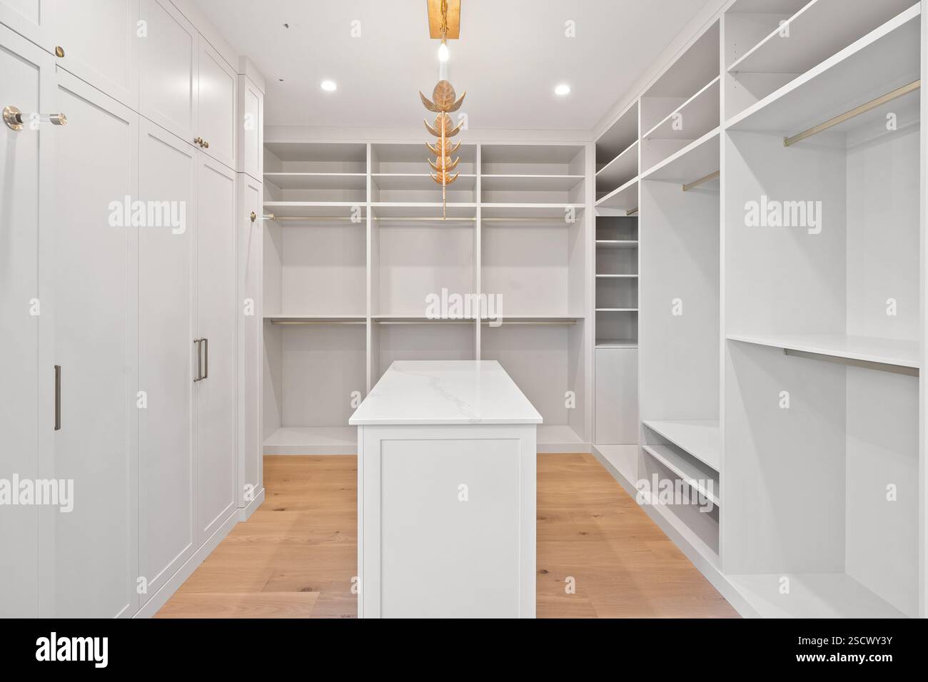 A large, empty walk in closet with white cabinets and a white counter ...