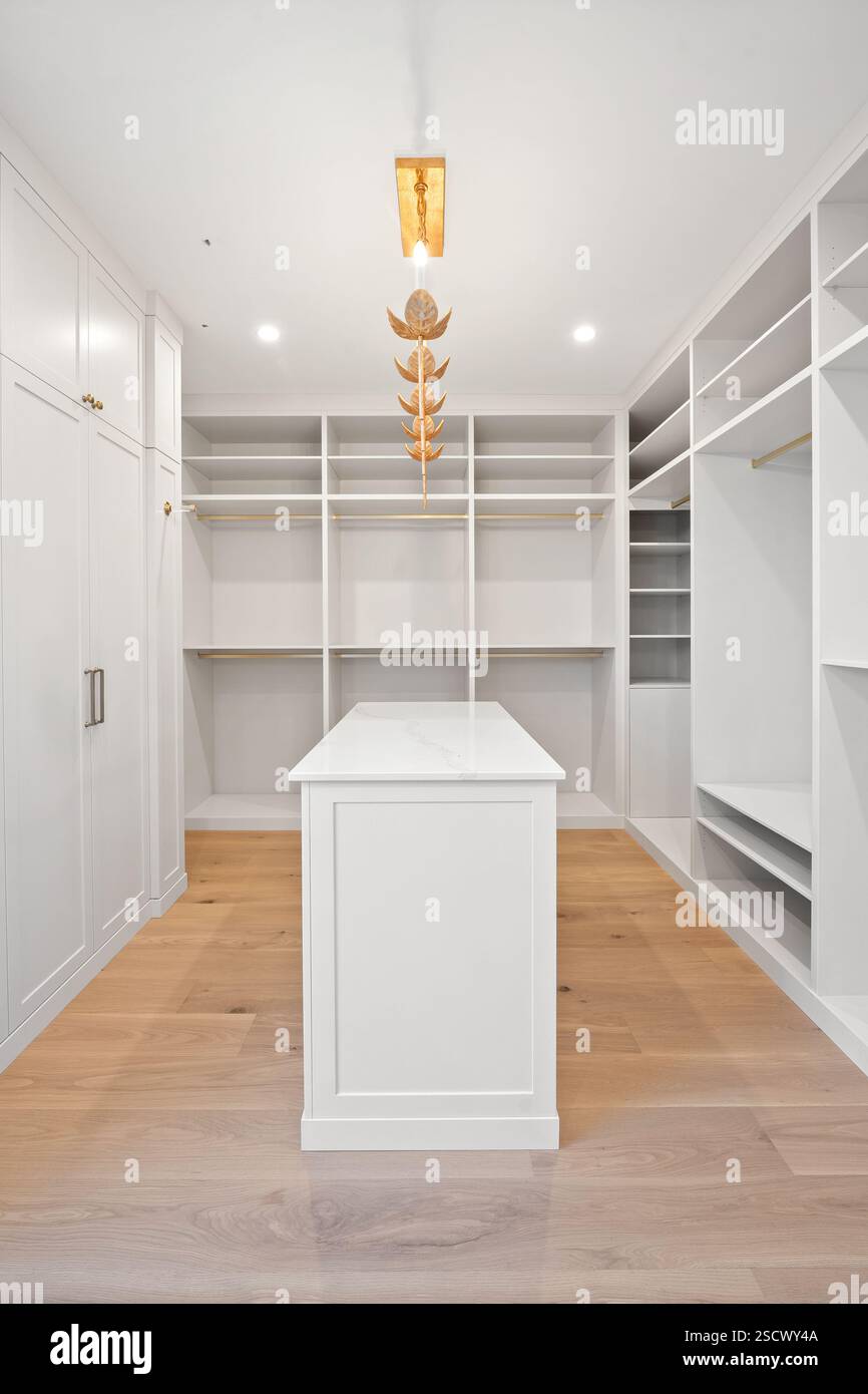 A large, empty walk in closet with a white counter and a hanging light ...