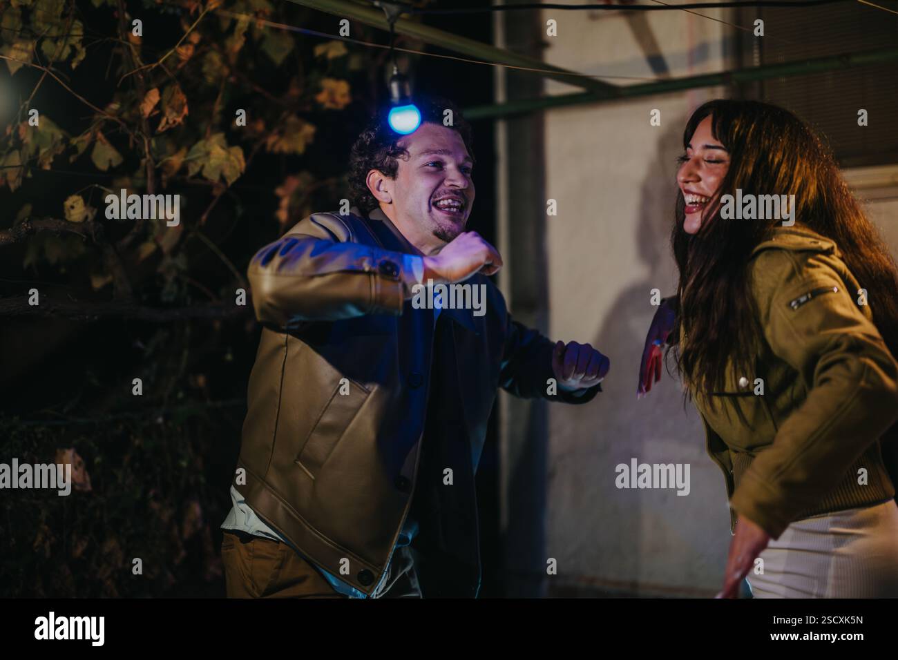 Two friends dancing joyfully together under lights at night outdoors ...