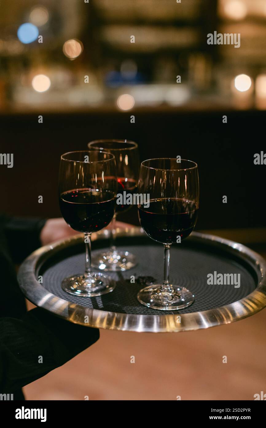 Waitstaff carries a silver tray with three glasses of red wine in a ...