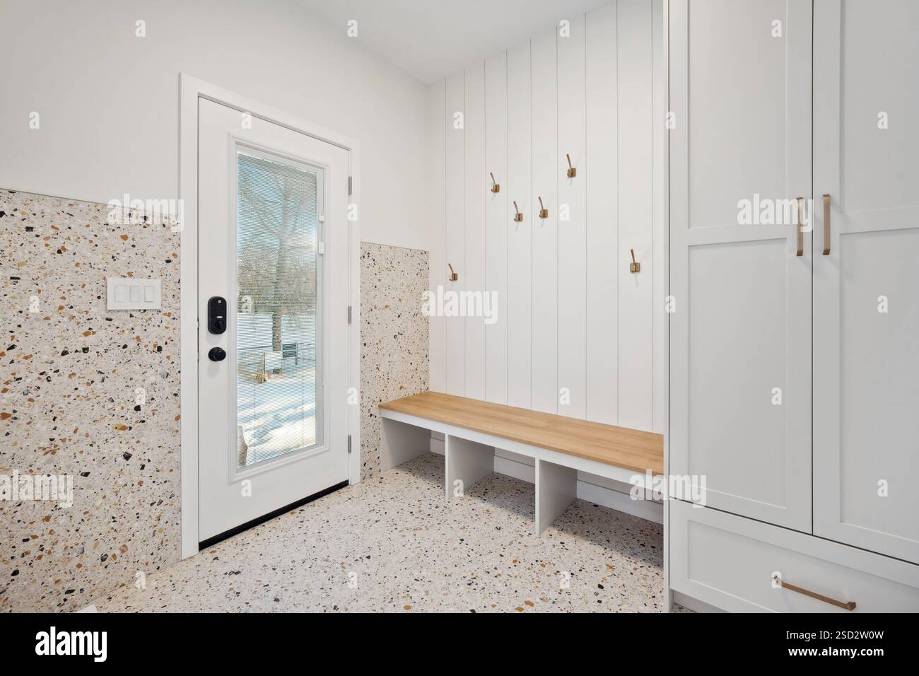 White and tan bathroom with a bench and a door. The bench is wooden and ...