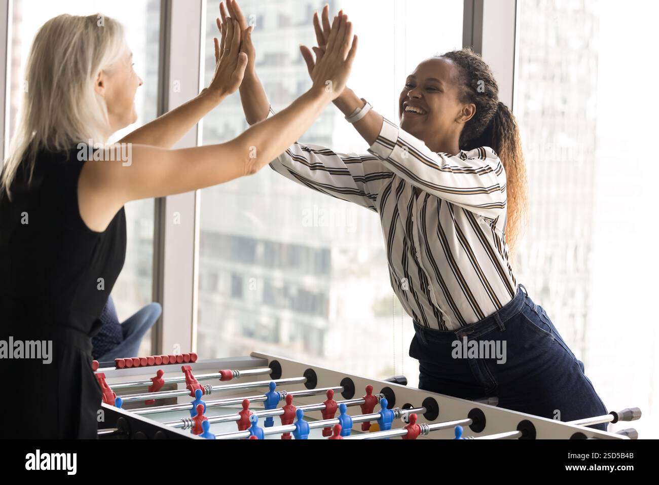 Colleagues playing table football, giving high five gesture, celebrate ...
