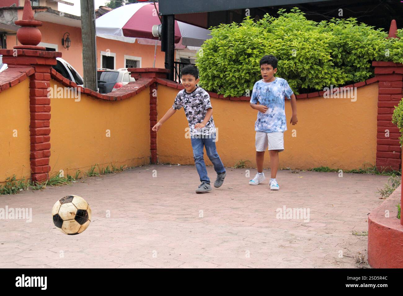 Two 9-year-old poor dark-skinned Latino boys play soccer in the street ...