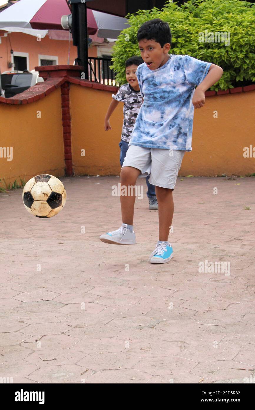 Two 9-year-old poor dark-skinned Latino boys play soccer in the street ...