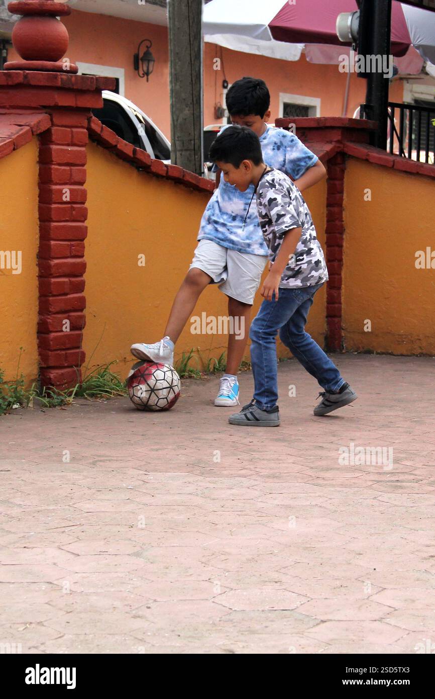 Two 9-year-old poor dark-skinned Latino boys play soccer in the street ...