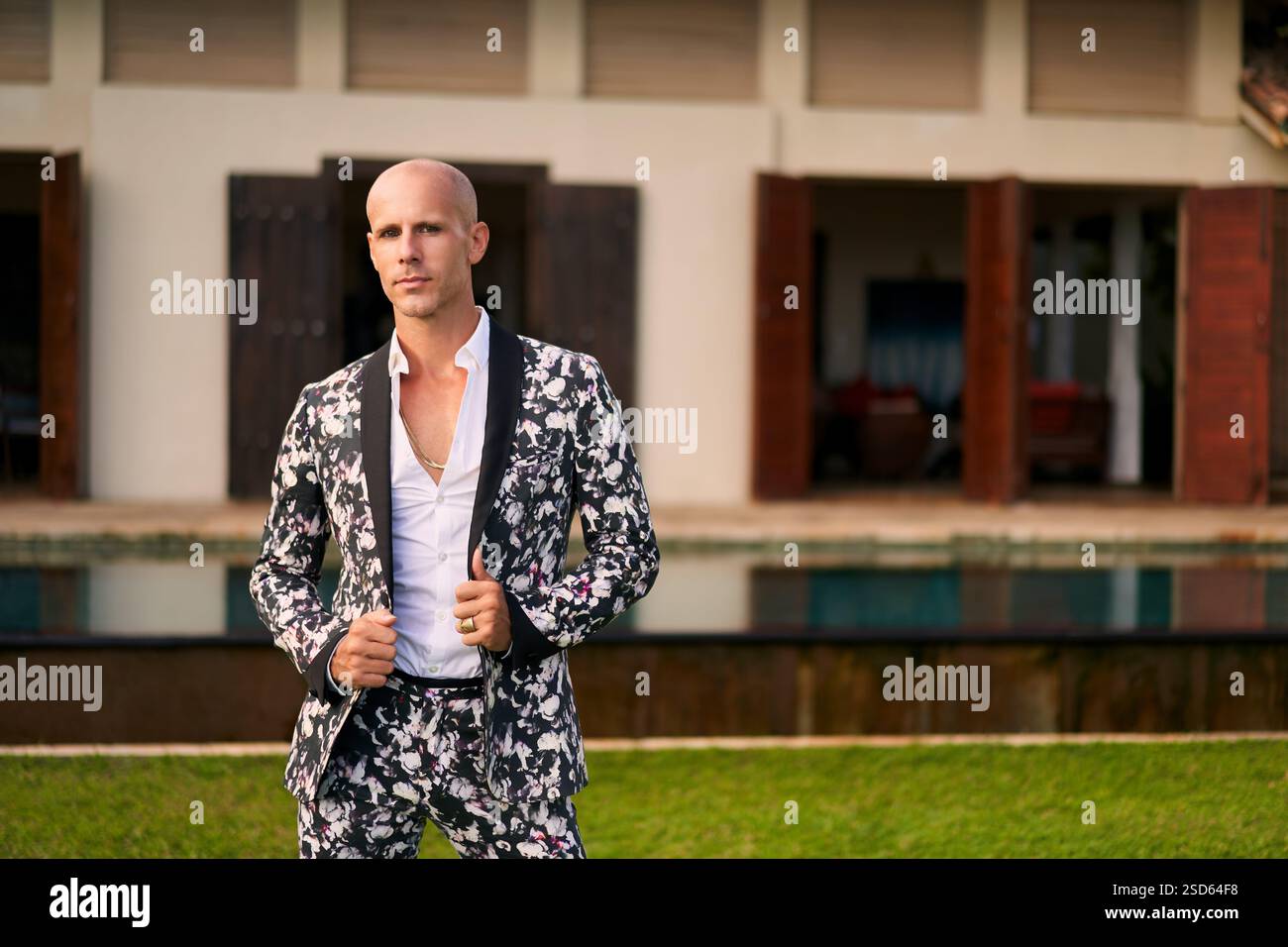 Bald man, bold floral suit poses villa courtyard. Stylish outfit ...