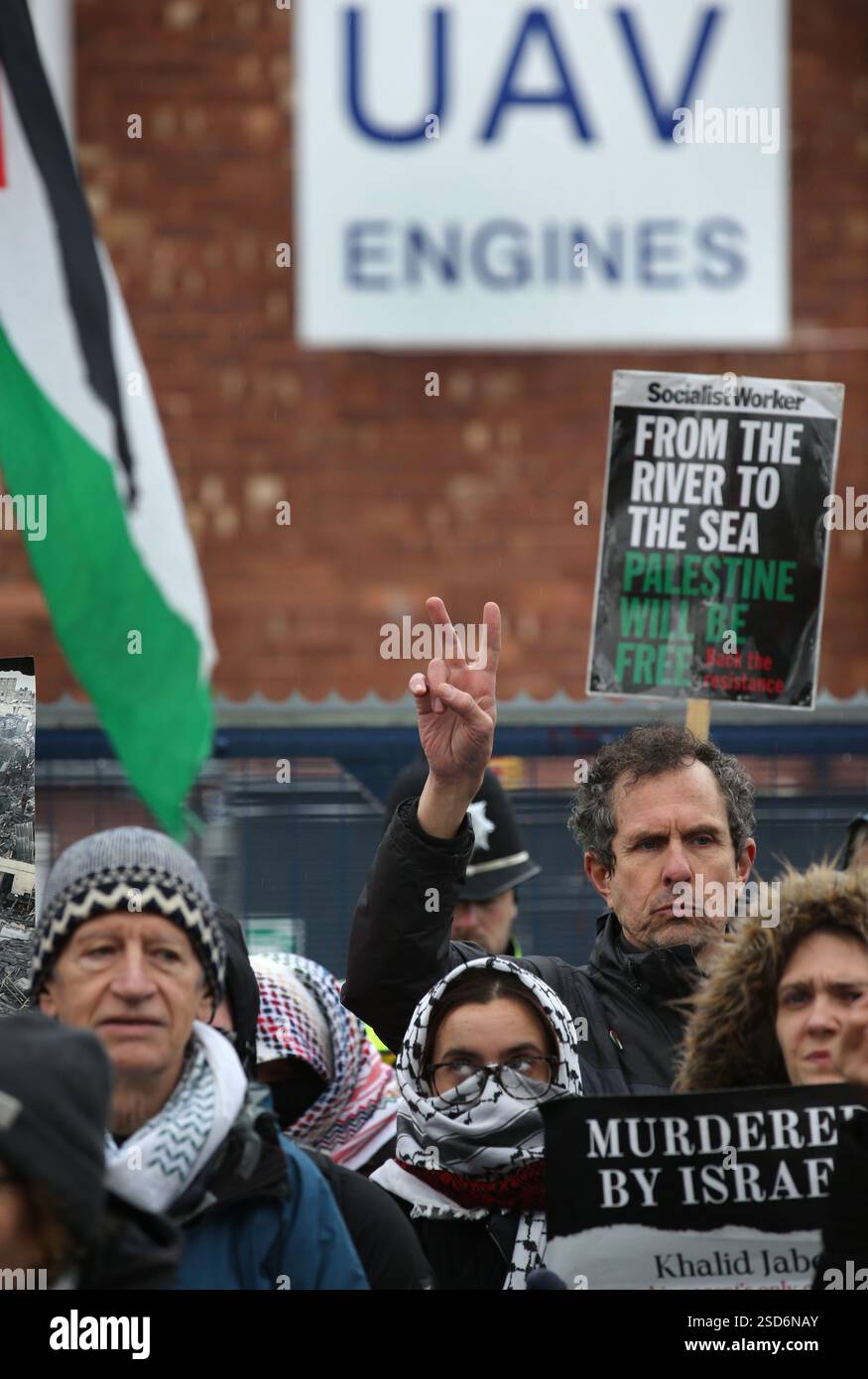 Protesters gather with posters as one gives a two-fingered peace sign ...