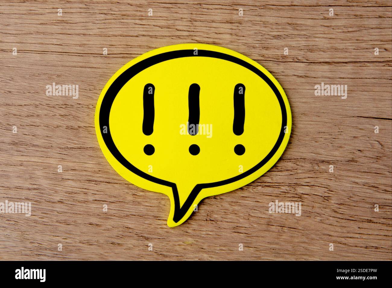 A yellow speech bubble with multiple exclamation marks on a wooden ...