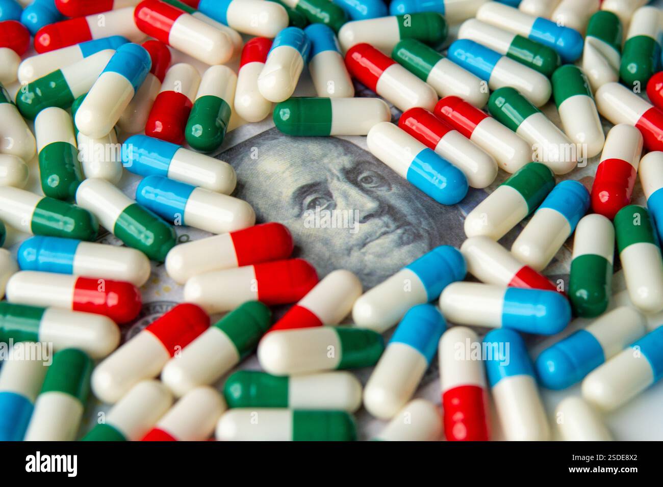 A close-up image of colorful capsules scattered on a US dollar bill ...