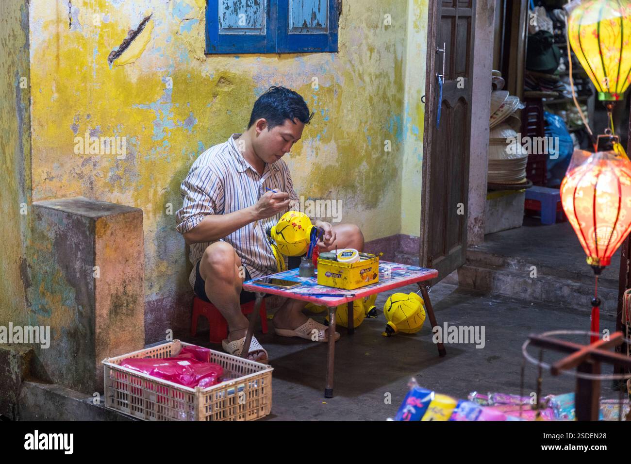 A young man carefully paints lanterns in an outdoor workshop in Hoi An ...