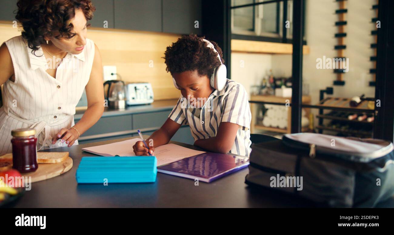 Mother, homework and child learning with headphones in kitchen for ...