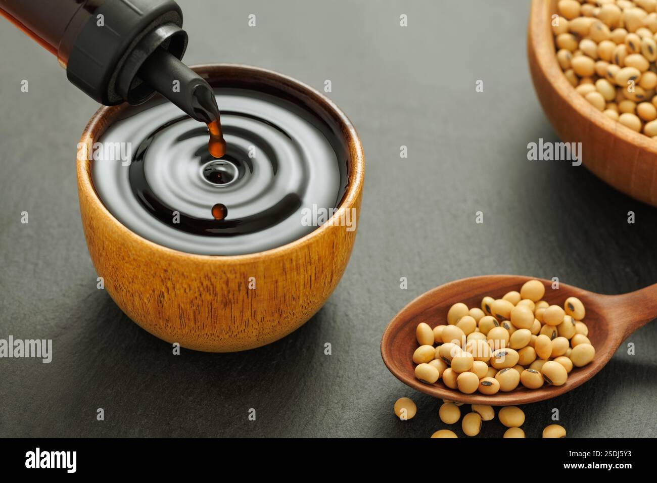soy sauce pouring from bottle in wooden bowl with splash and drop and ...