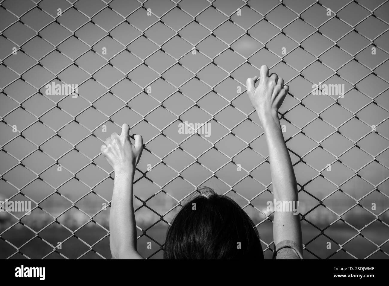 Closeup of a human hand gripping a chain link fence as if trying to escape, representing border ...