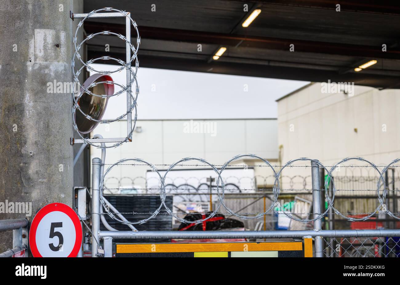 Razor and barbed wire topping a security fence. 5 kmh speed limit sign ...