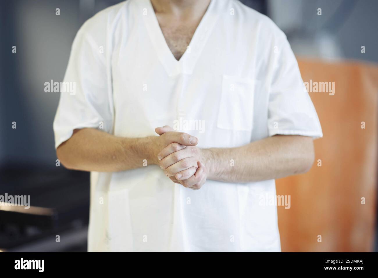 A man in a white hospital gown with hands clasped, conveying calmness ...