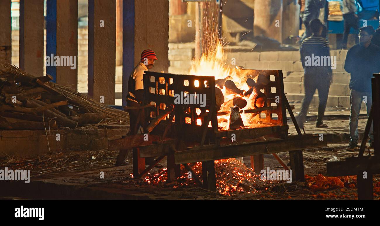 Varanasi, Uttar Pradesh, India. Indian worker man helps a fire burn ...
