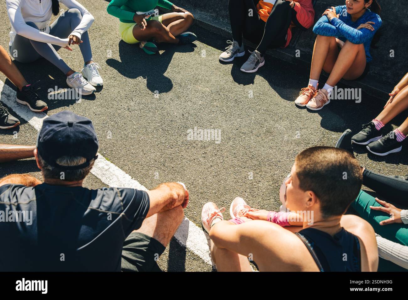 A diverse group of running club members sits together on a sunny day ...
