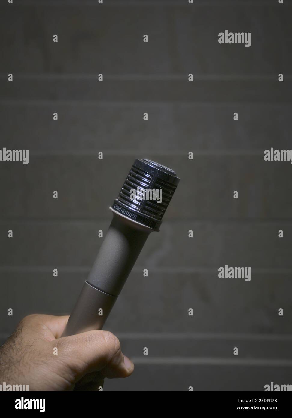 hand holding condenser microphone under spot light against a dark ...