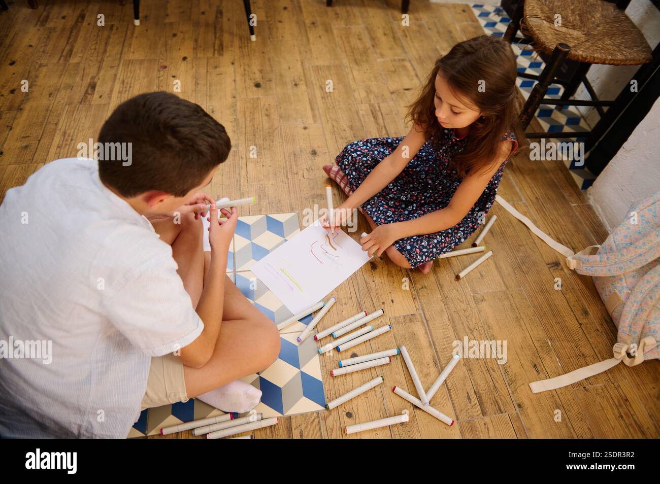 Two children are creating art together indoors, using markers and paper ...