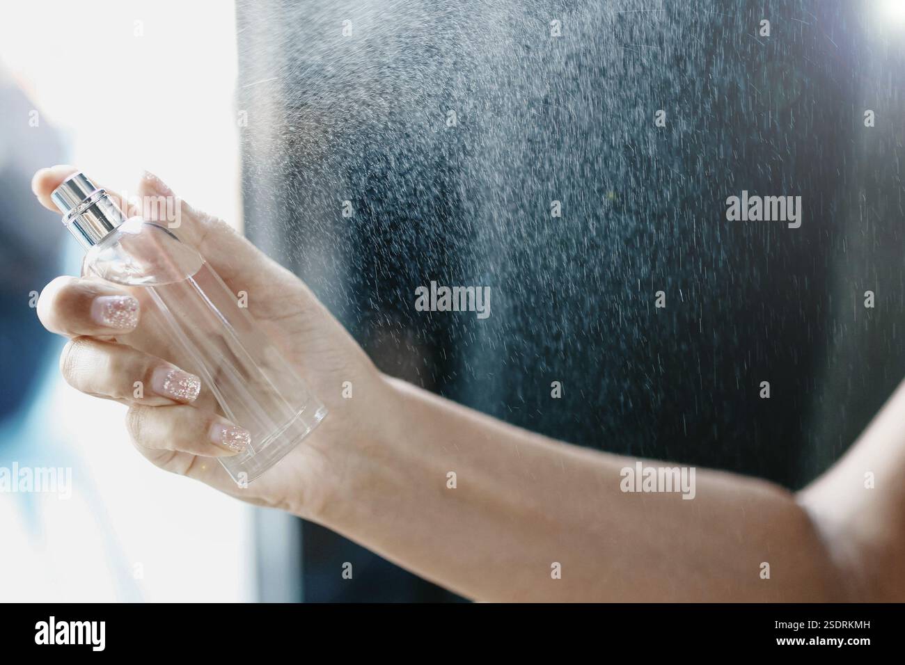 Hand spraying perfume from a glass bottle, creating a fine scent mist ...