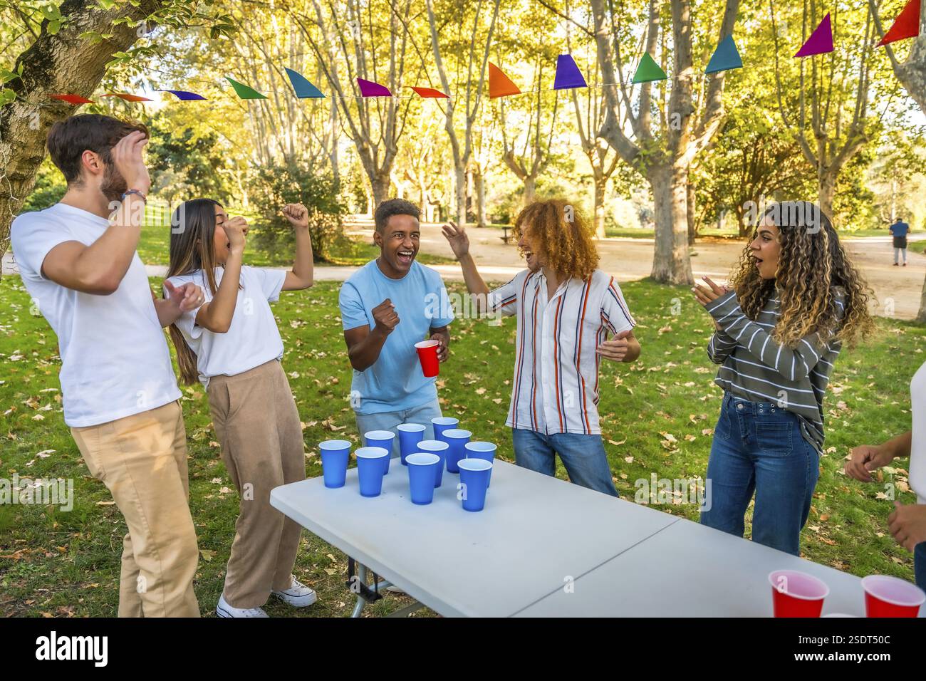 Diverse happy friends playing beer pong in a park while celebrating ...