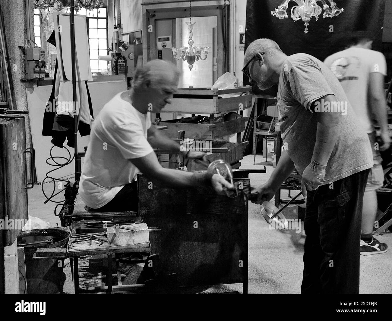 Two artisans craft glass in a workshop using traditional techniques ...