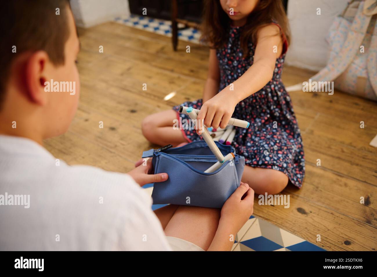 Two kids sitting on the floor as they arrange and organize markers ...