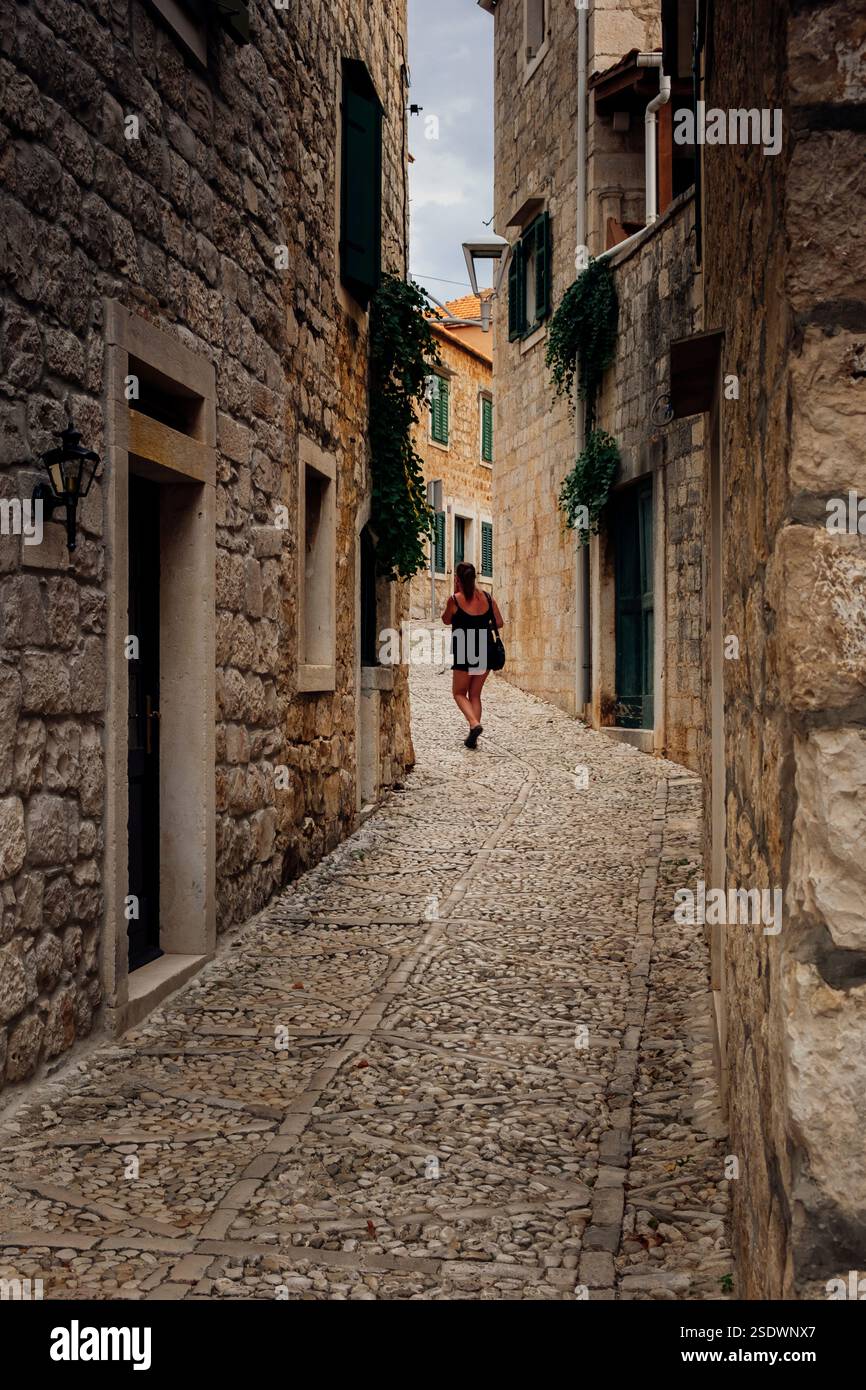 Solo female tourist in intricately pebbled alleys of Old Town Postira ...