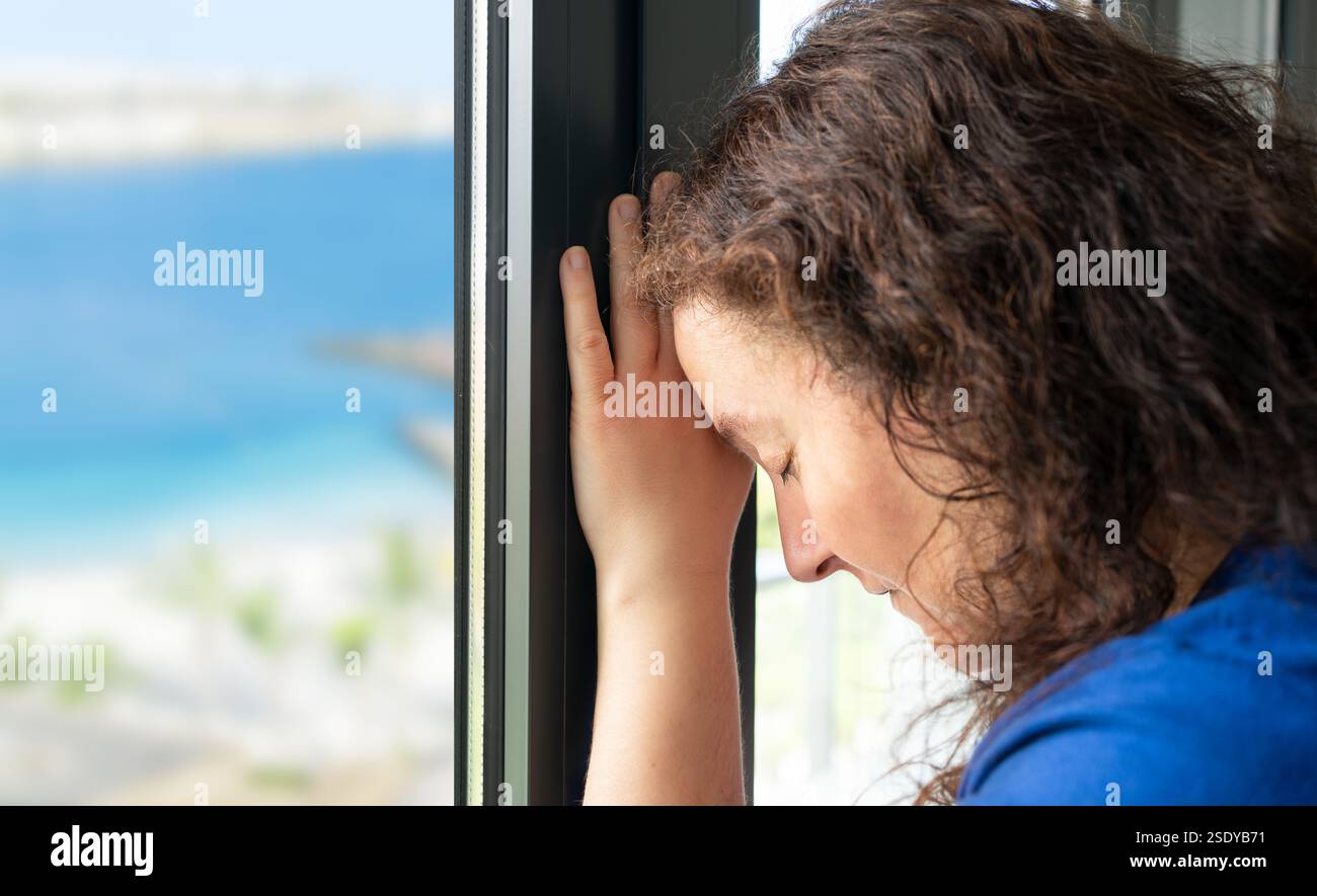 Side view portrait of a sad single woman looking down from a window of ...