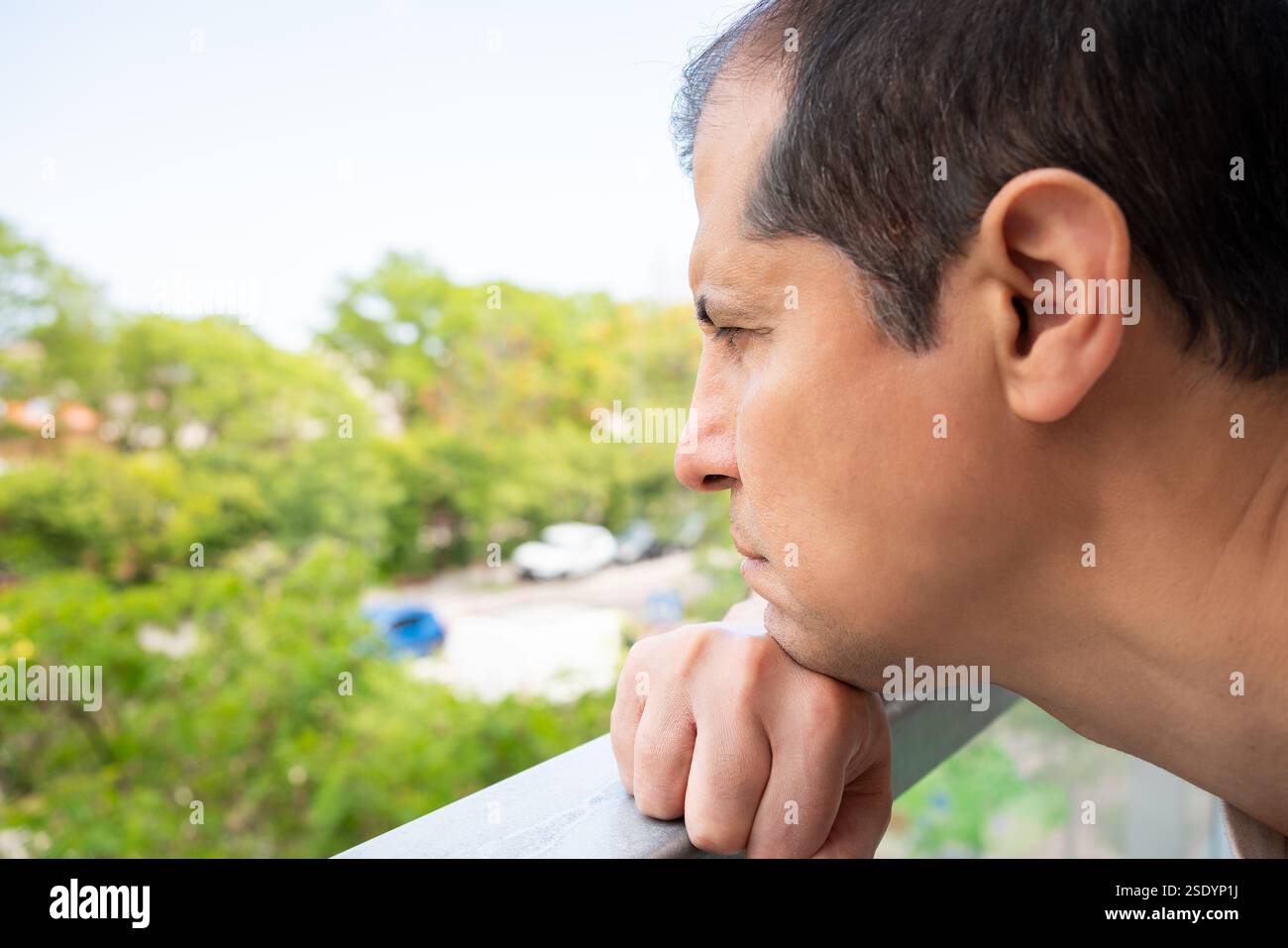 Side view portrait of a sad single man looking down from a balcony of a ...