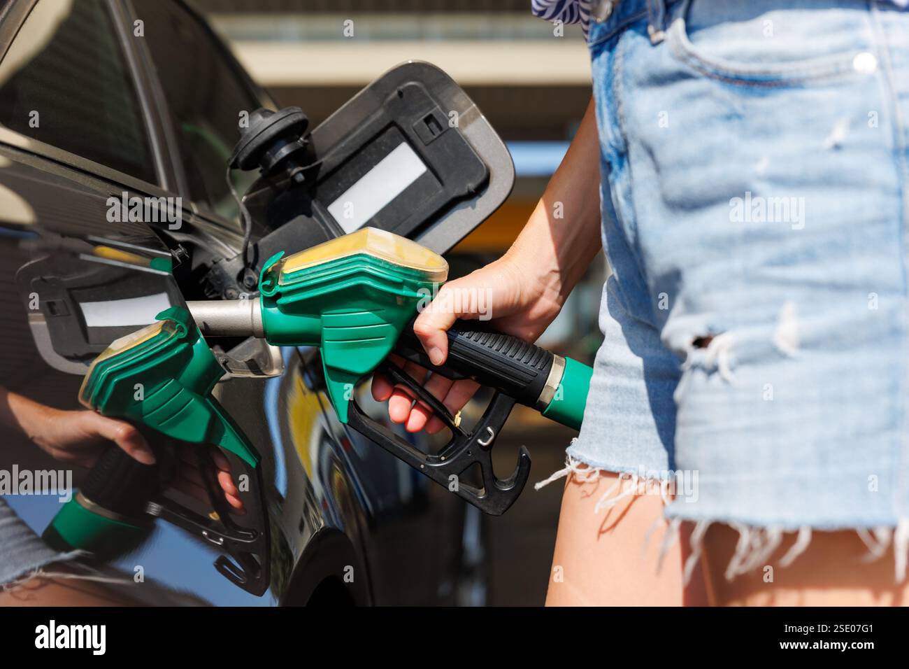 Close--up woman casual outfit hand hold fuel pump nozzle refuel car gas ...