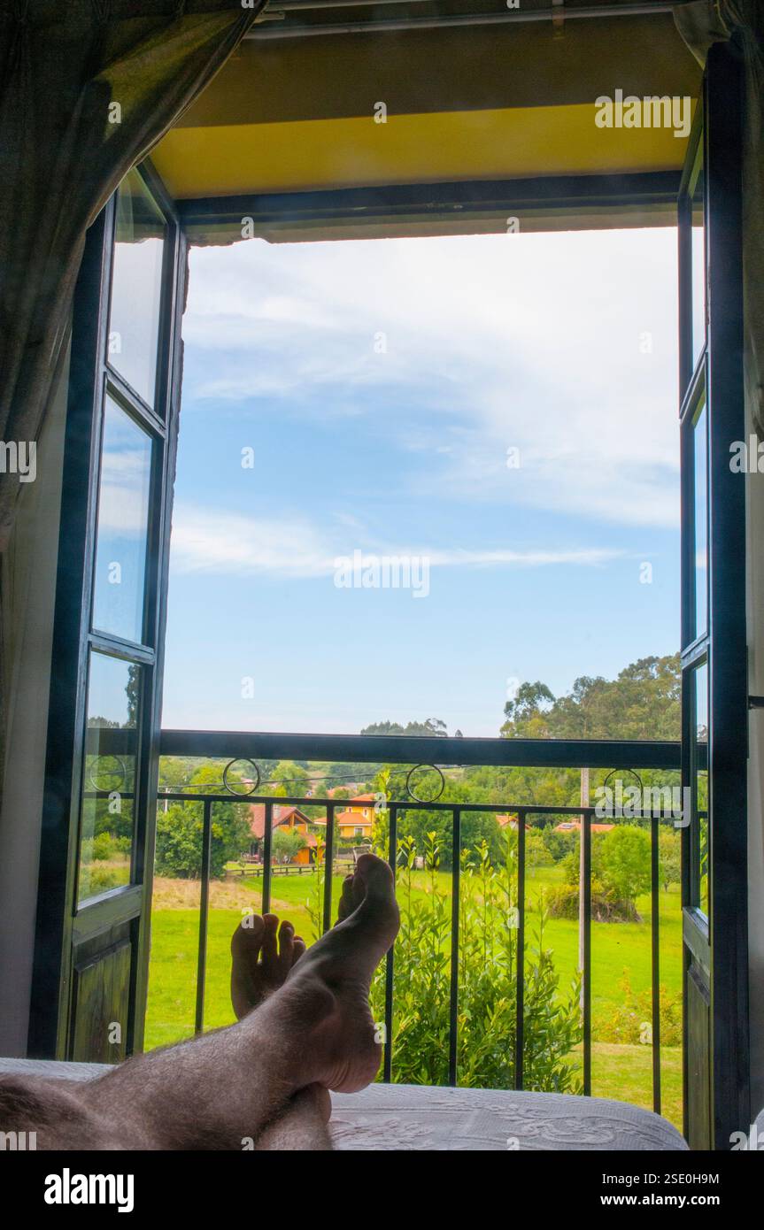 Man's feet lying on bed by an open window in rural house. Asturias ...