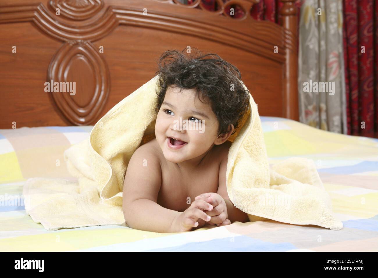 One and half year old baby sleeping on stomach on bed with yellow towel ...