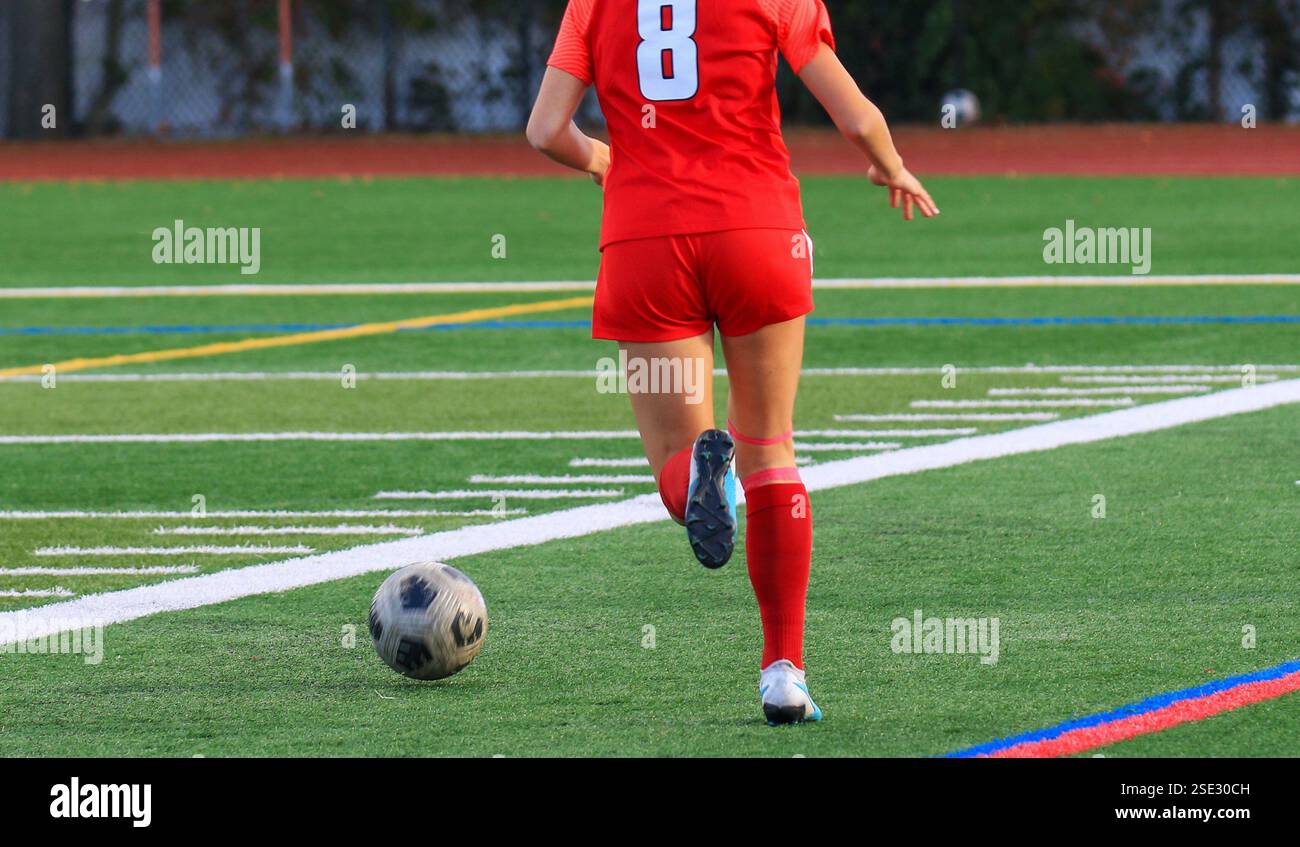 A female soccer player in a red uniform runs quickly toward the ball on ...