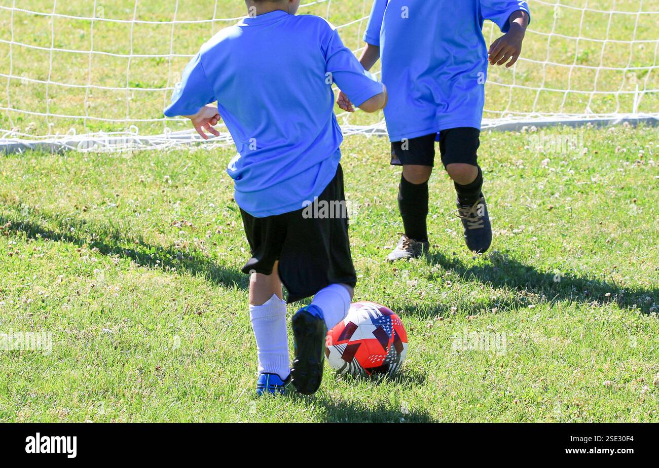 Two boys dribble a soccer ball across a grassy field, focusing on their ...