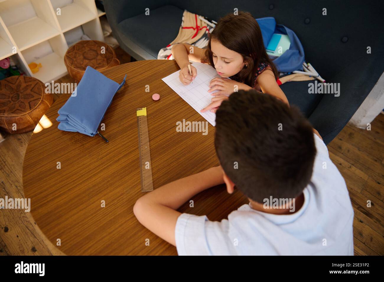 Two children work on their homework at a round wooden table. The scene ...