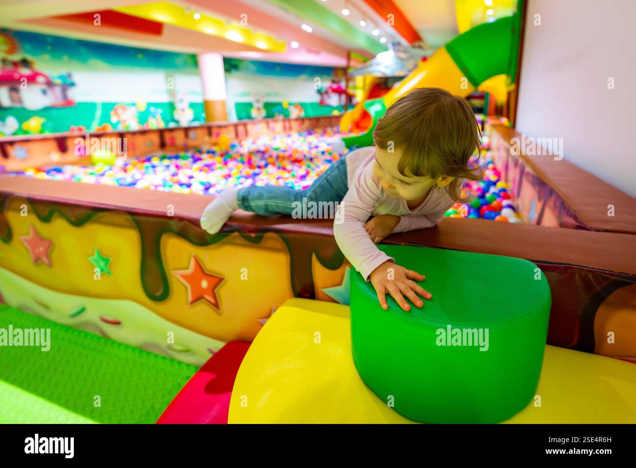 A curious child climbing over a colorful barrier in a lively indoor ...