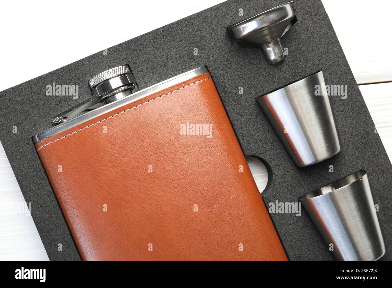 Hip flask, cups and funnel in package on white wooden table, top view ...