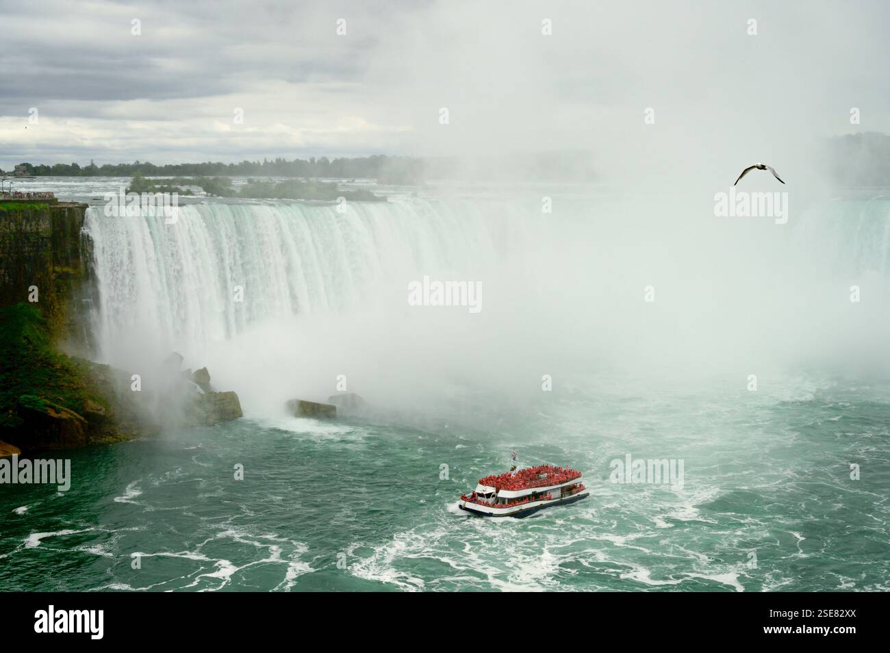 Powerful waterfalls cascade dramatically as a boat tour approaches ...
