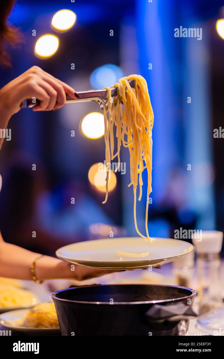 A person serves cooked spaghetti onto a plate in a brightly lit dining ...