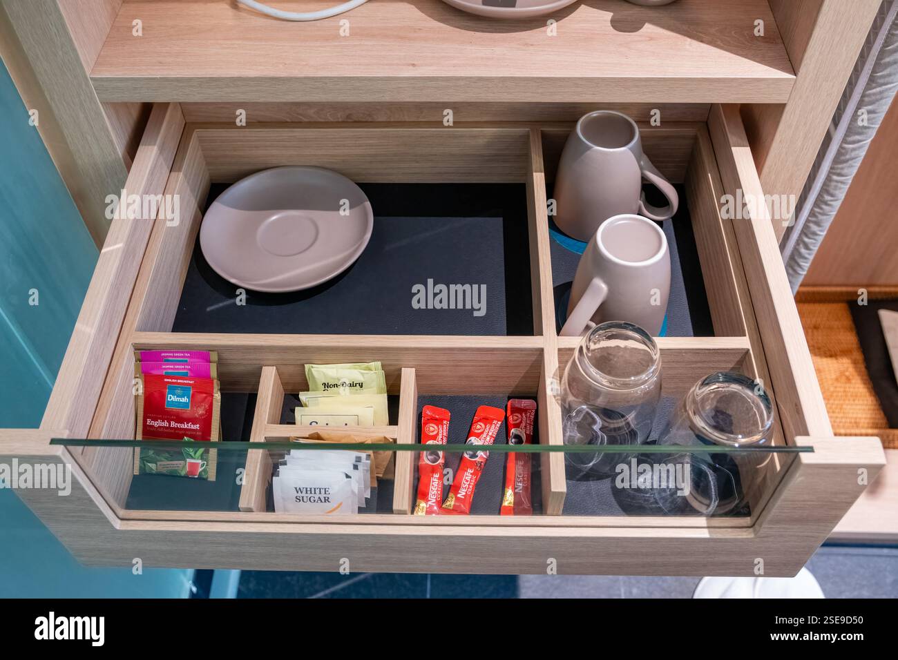 Organized drawer with tea bags, coffee sachets, sugar, ceramic mugs ...