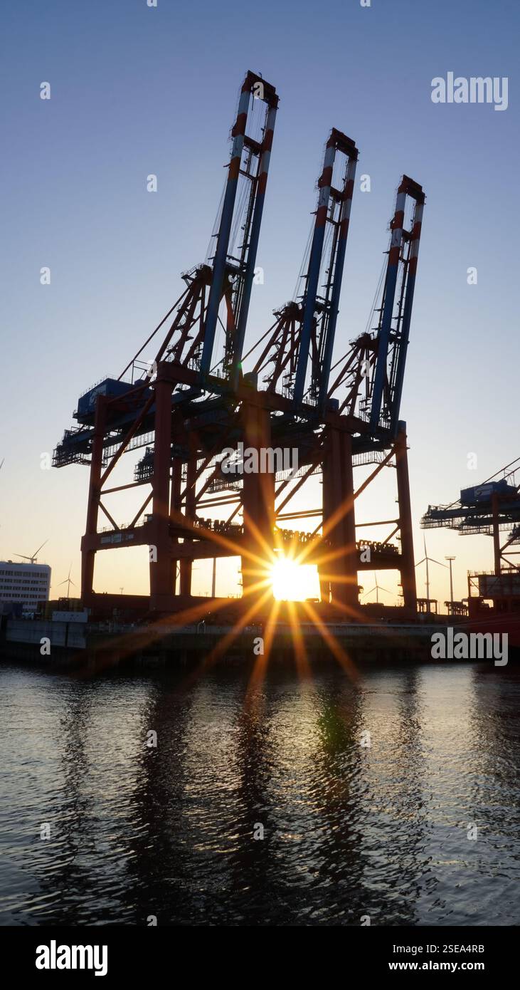 Three folded up container bridges in the low evening sun with sun star ...