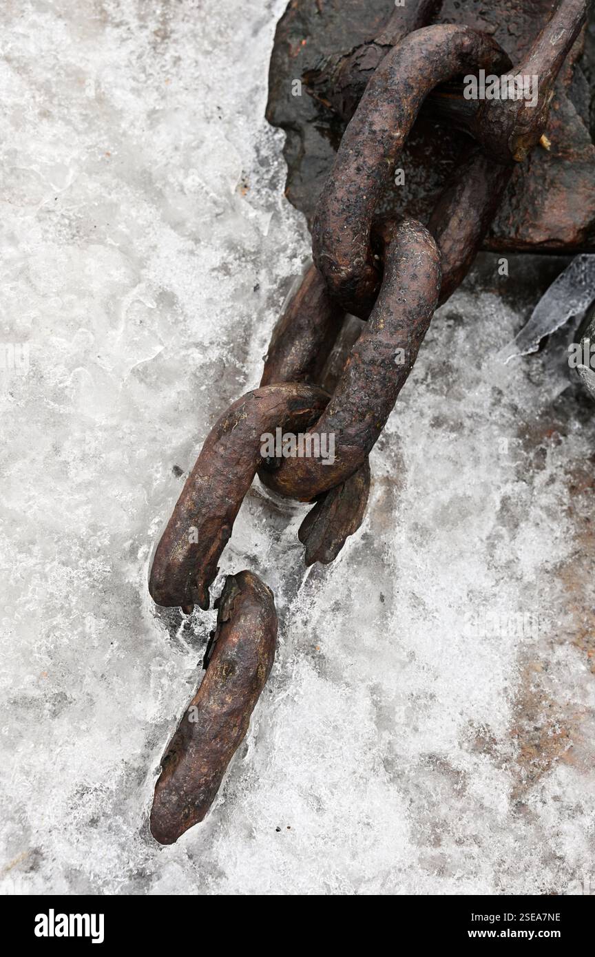 A heavily rusted, broken chain lies partially submerged in ice, its ...