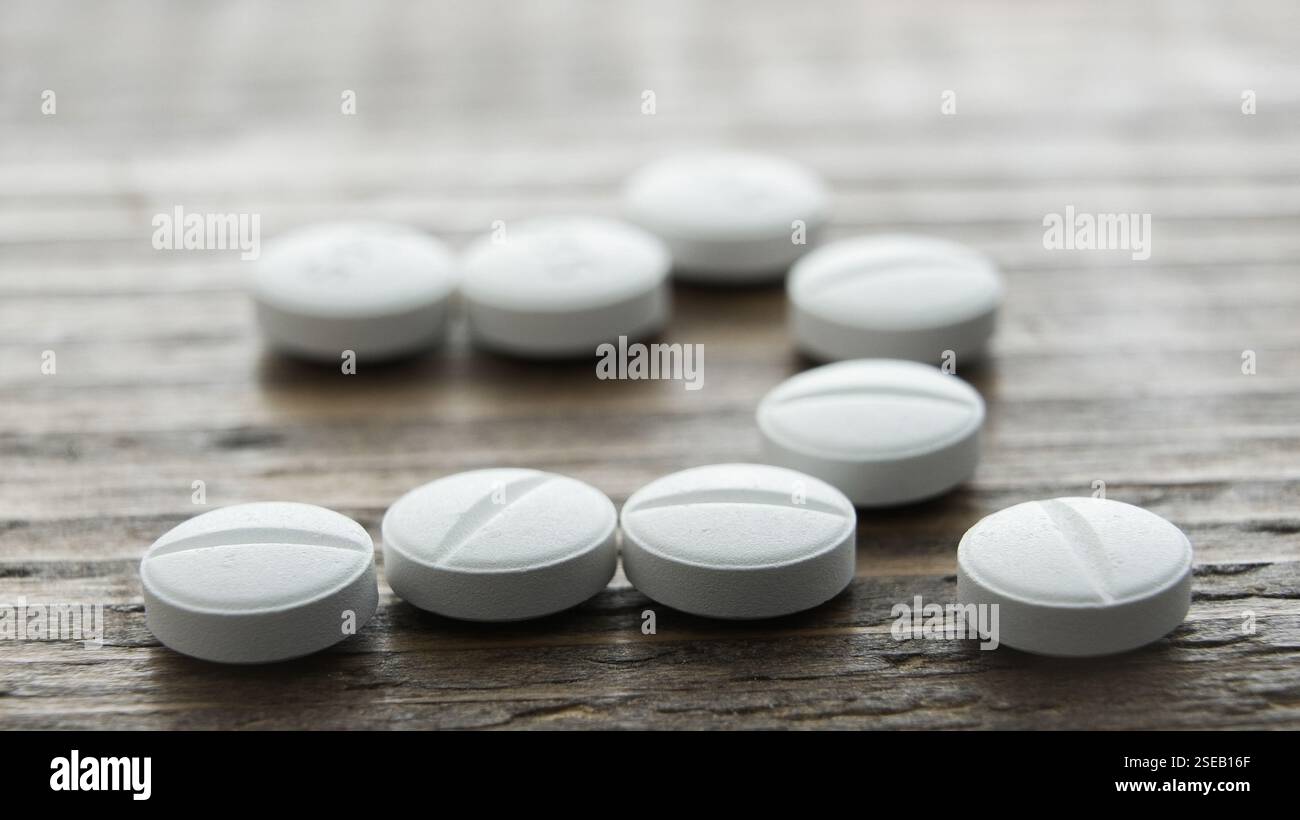 White tablets are carefully lined up on a textured wooden surface ...