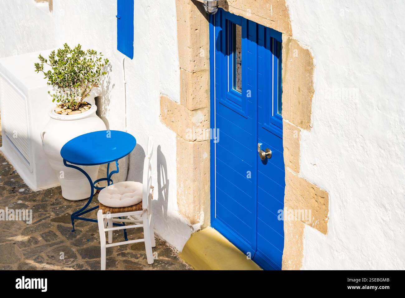 Typical white Greek house with blue door and small table with chair in ...