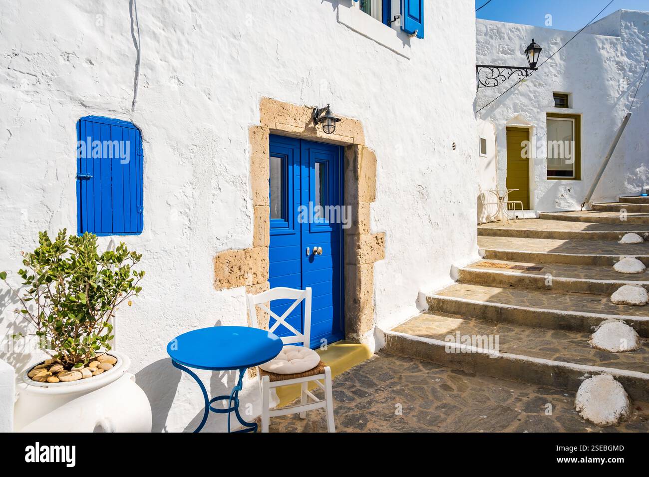 Typical white Greek house with blue door and small table with chair on ...